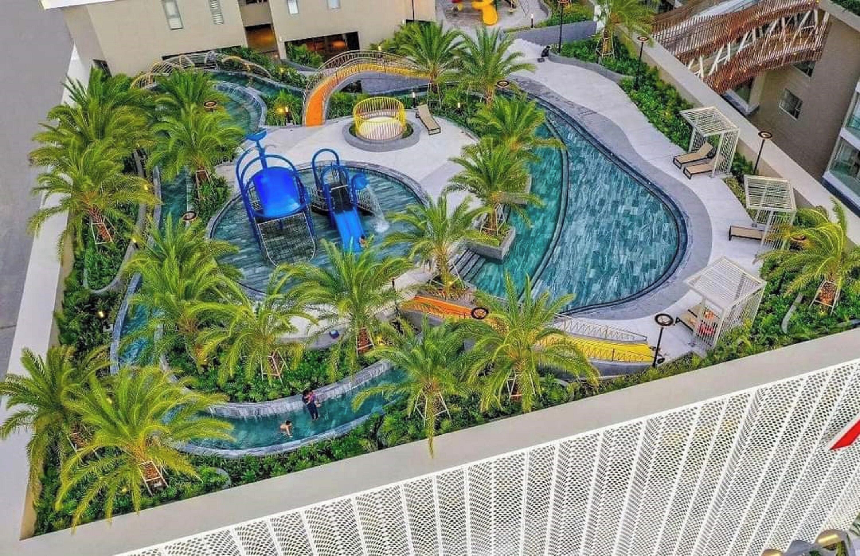 Uma área de piscina no terraço com um escorregador azul, palmeiras e cadeiras de descanso.