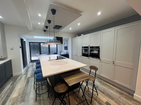 Cozinha moderna com ilha central, banquetas e fornos embutidos.