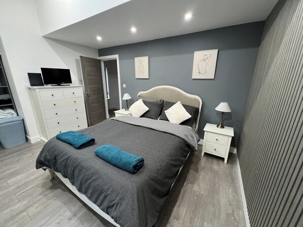 Quarto moderno com cama, mesas de cabeceira, televisão e guarda-roupa.