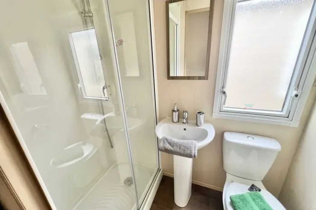 Um banheiro com box de vidro, pia de pedestal, vaso sanitário e janela.
