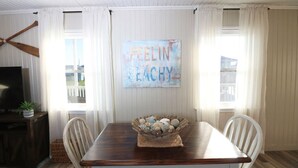 Uma área de refeições com uma mesa de madeira, duas cadeiras brancas, uma tigela decorativa e uma parede com o letreiro 'FEELIN'.