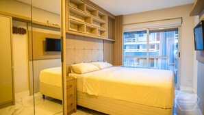Quarto com cama grande, estantes embutidas, televisão e porta de correr para uma varanda.