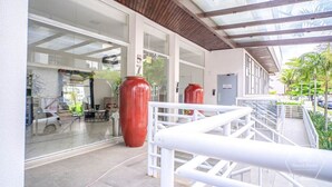 Um edifício moderno com grandes janelas, área externa coberta e objetos cilíndricos vermelhos.