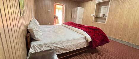 Quarto de hotel com uma cama, um guarda-roupa, uma pequena prateleira e uma porta que dá para outro aposento.