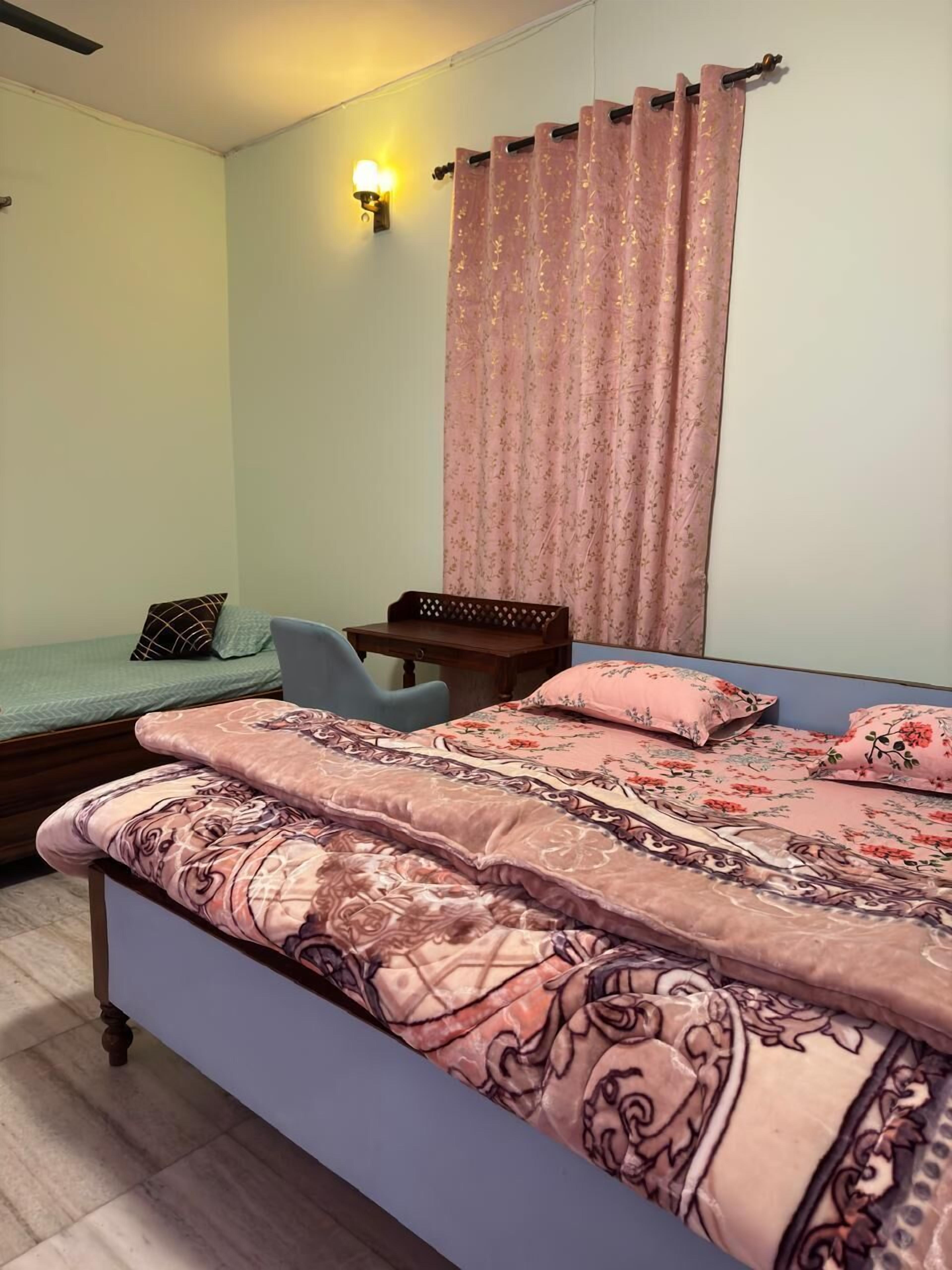 Quarto com cama, escrivaninha, cadeira e luminária fixada na parede.