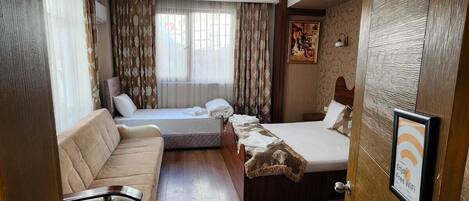 Quarto de hotel com sofá, duas camas, uma luminária no teto e uma porta com placa oferecendo Wi-Fi gratuito.