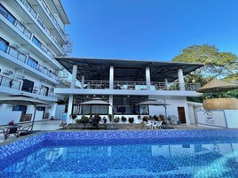 Um hotel com piscina, área de estar externa e terraço coberto.