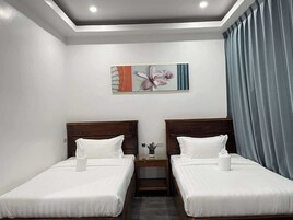 Quarto de hotel com duas camas de solteiro, uma pequena mesa de cabeceira com um vaso e um quadro na parede.