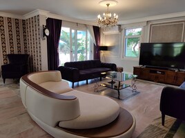 Uma sala de estar com sofá, poltrona, mesa de centro, televisão e lustre.