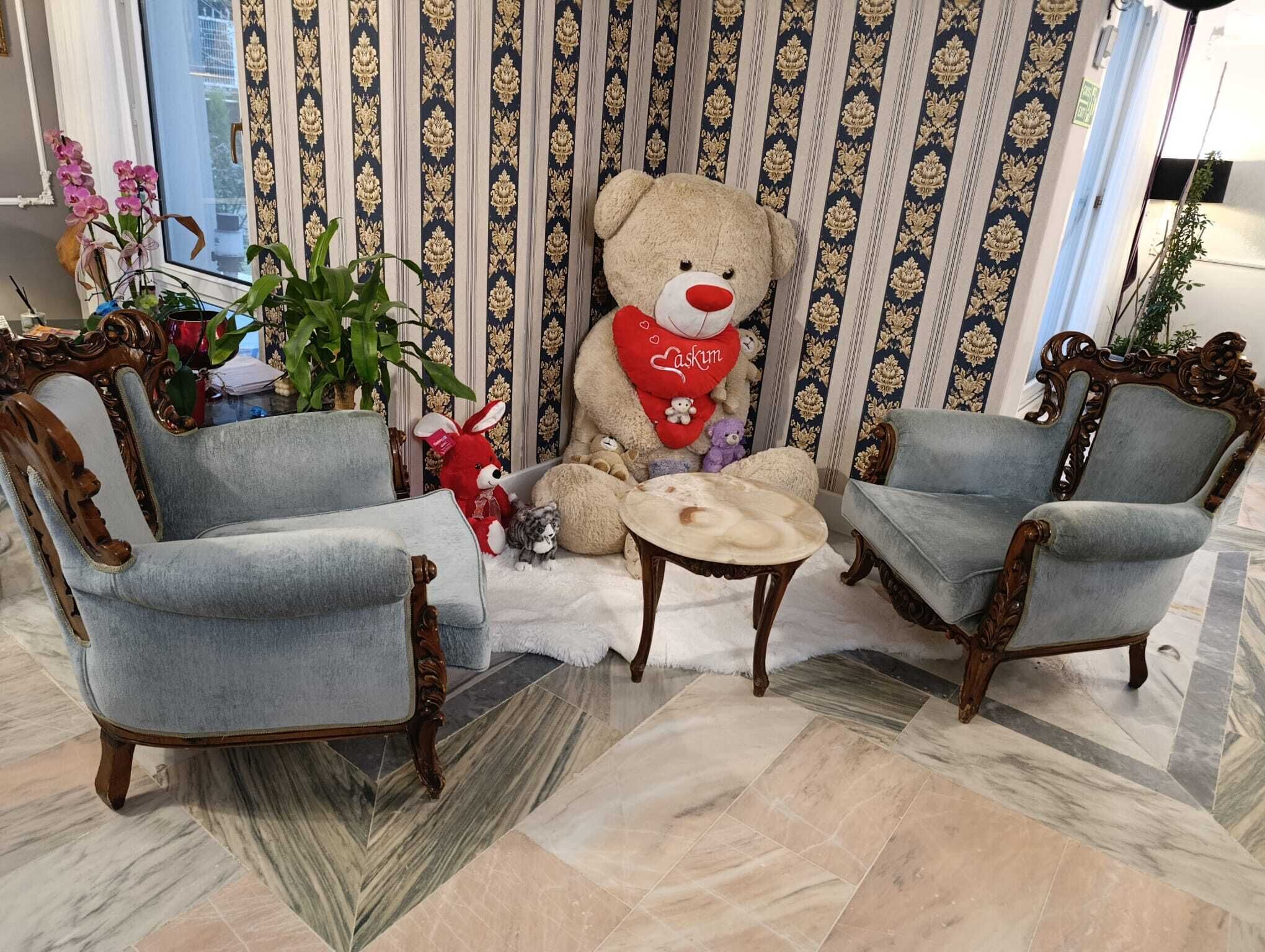 Quarto com duas poltronas estofadas, uma mesinha redonda e um urso de pelúcia grande com almofada em formato de coração.