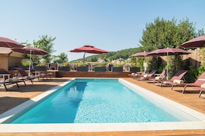 Piscina retangular com espreguiçadeiras e guarda-sóis em um deck de madeira.
