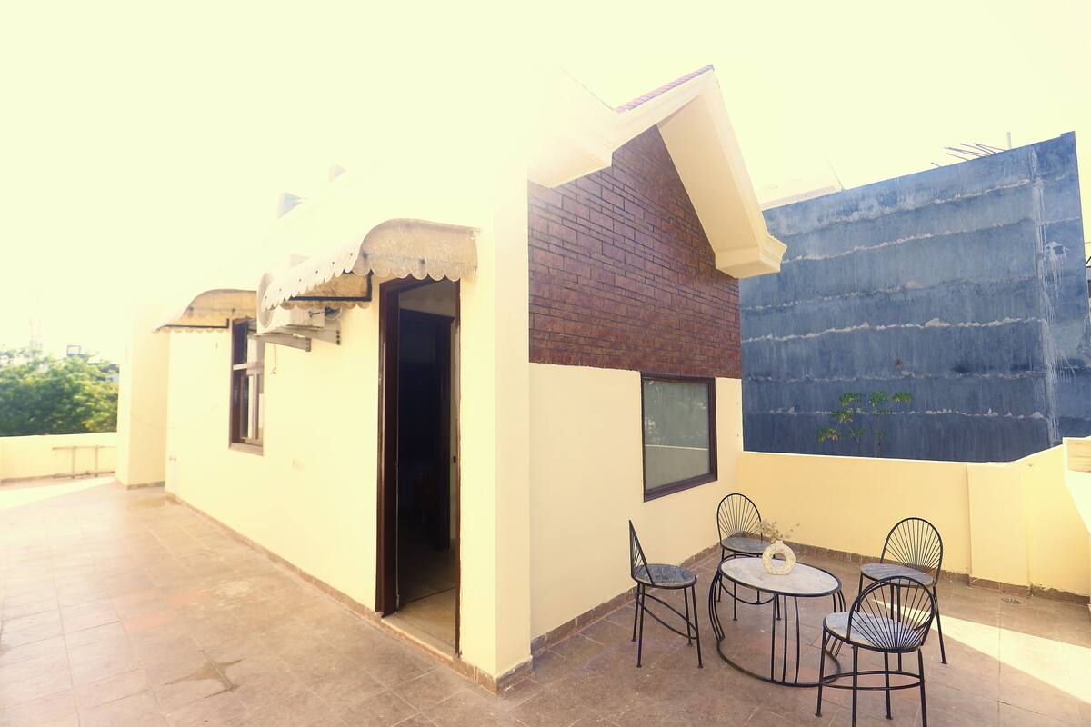 Terraço no telhado com uma mesa pequena, cadeiras, uma janela e uma porta.
