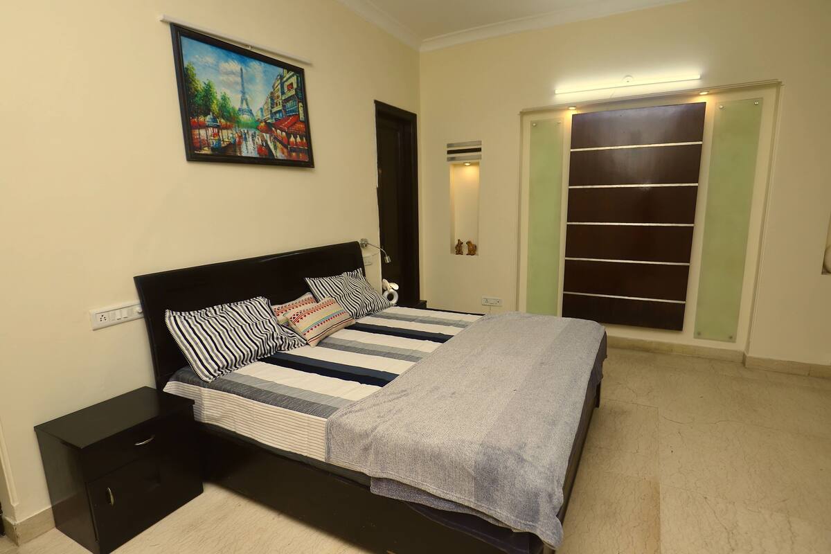 Quarto com cama, mesa de cabeceira, penteadeira, quadro e guarda-roupa com porta deslizante.