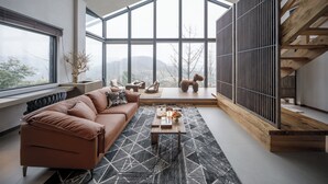Uma sala de estar moderna com uma janela grande, um sofá marrom, uma mesa de centro e uma escada de madeira.