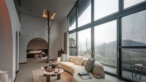 Sala de estar moderna com uma janela grande, um sofá, uma mesa de centro e uma cama ao fundo.