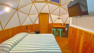 Quarto tipo tenda com cama, TV e uma pequena cozinha.