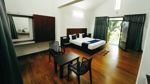 Quarto de hotel com cama, escrivaninha, duas cadeiras, guarda-roupa e porta de vidro que dá para uma varanda.