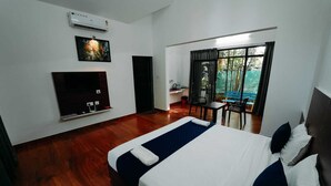Quarto de hotel com uma cama grande, televisão de tela plana, uma mesinha e uma janela com vista para vegetação.