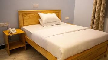 Uma cama de solteiro com cabeceira de madeira e roupa de cama branca num quarto com paredes azul claro e cortina estampada.