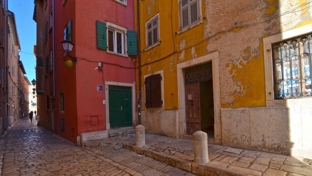 Uma rua estreita de paralelepípedos, com edifícios pintados de vermelho e amarelo.