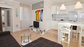 Um apartamento moderno com sala de estar, área de refeições e cozinha. Há uma televisão, uma mesa de centro de vidro e um sofá.