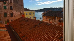 Vista da janela com vista para um rio e prédios, incluindo um edifício amarelo e um prédio de pedra com telhado de azulejos.
