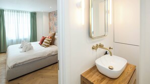 Quarto de hotel com uma cama, uma toucador de madeira com uma pia branca e um espelho grande.