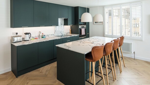 Uma cozinha moderna com armários verde-escuros, bancada de mármore e uma ilha central com banquetas.