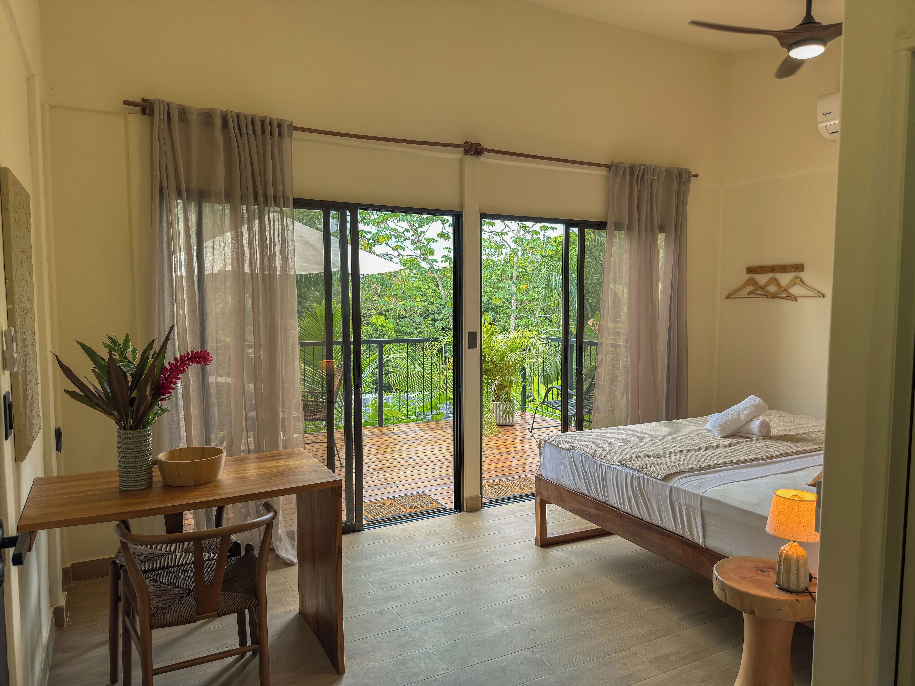 Quarto com cama, escrivaninha e cadeira. Possui uma varanda com vista para área verde.