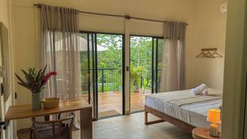 Quarto com cama, escrivaninha e cadeira. Possui uma varanda com vista para área verde.