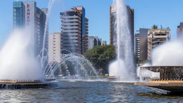 Paisagem urbana com uma fonte central rodeada por edifícios altos, incluindo um edifício com a sinalização 'RAMADA'.