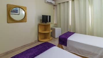Quarto de hotel com duas camas, televisão, pequena estante de madeira, ar condicionado e janela com cortinas.