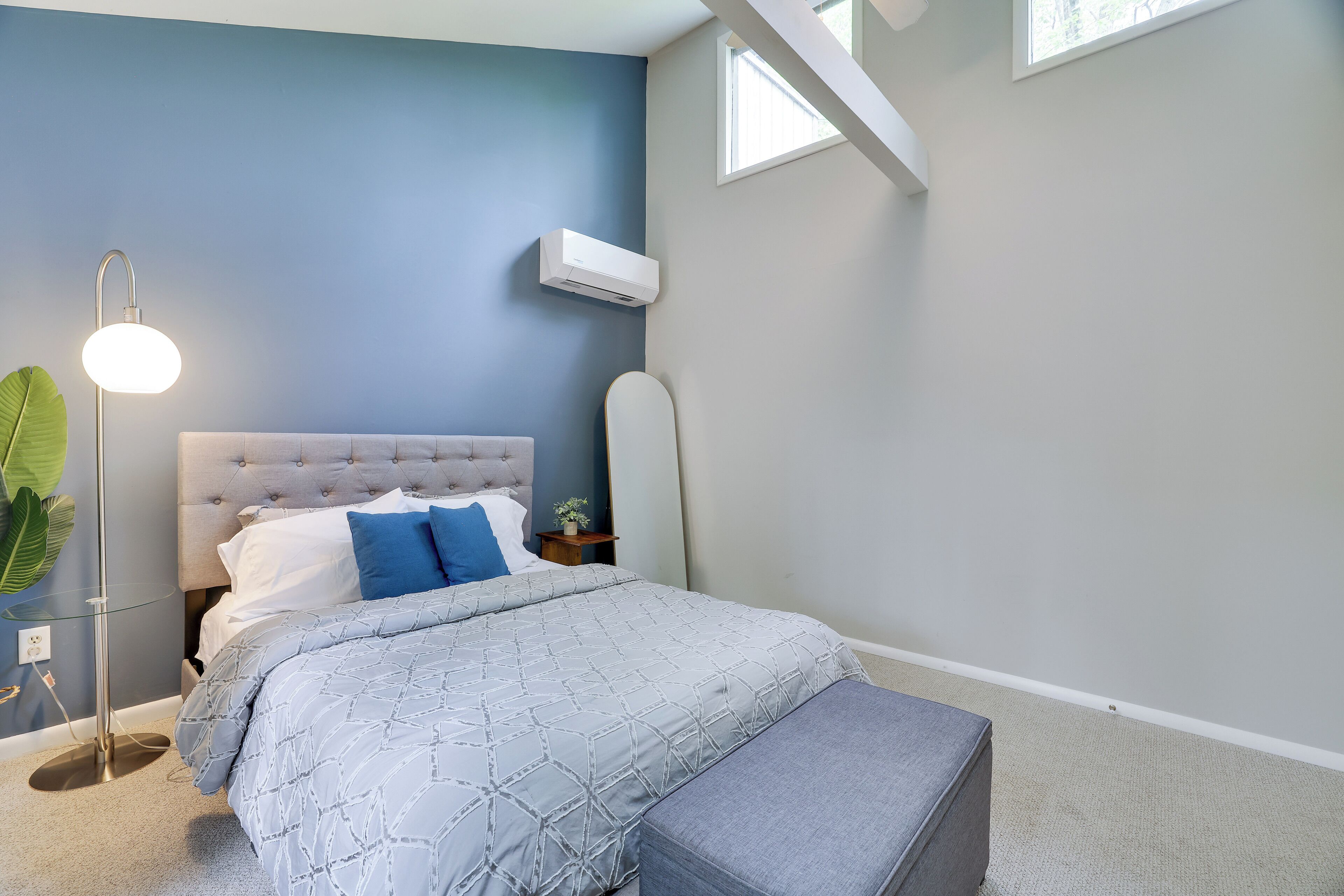 Quarto com cama, luminária de cabeceira, aparelho de ar condicionado e janela.