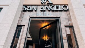 Exterior do Hotel San Angelo, com uma placa de destaque e uma entrada moderna.