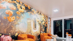 Quarto com mural de flores e janela, mobiliário laranja e mesa redonda com um vaso.