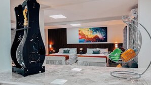Quarto de hotel com bancada de mármore, cama com roupa de cama branca, pintura abstrata colorida na parede e um porta-bagagem com malas.