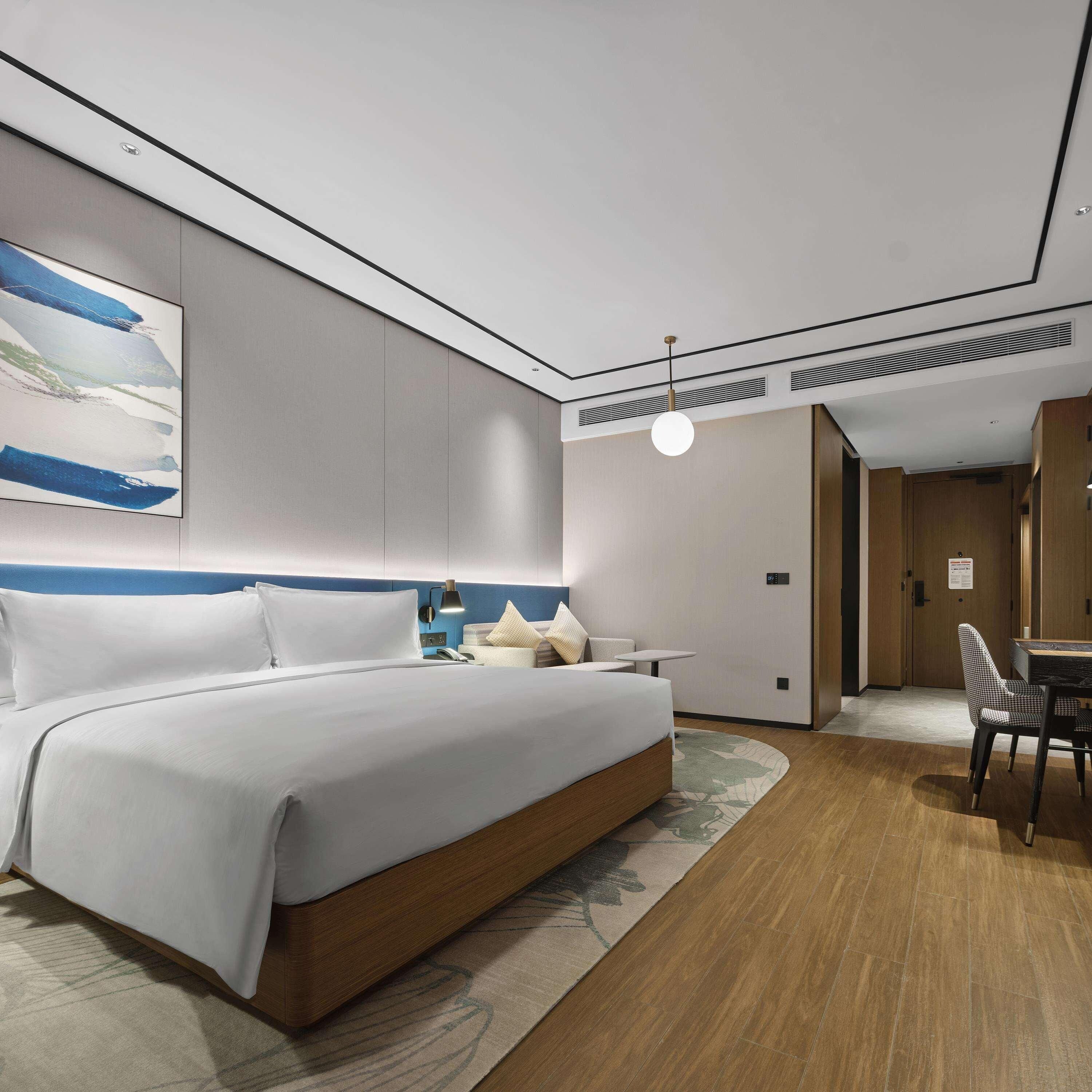 Quarto de hotel moderno com uma cama grande, mesas de cabeceira, uma escrivaninha e uma cadeira.