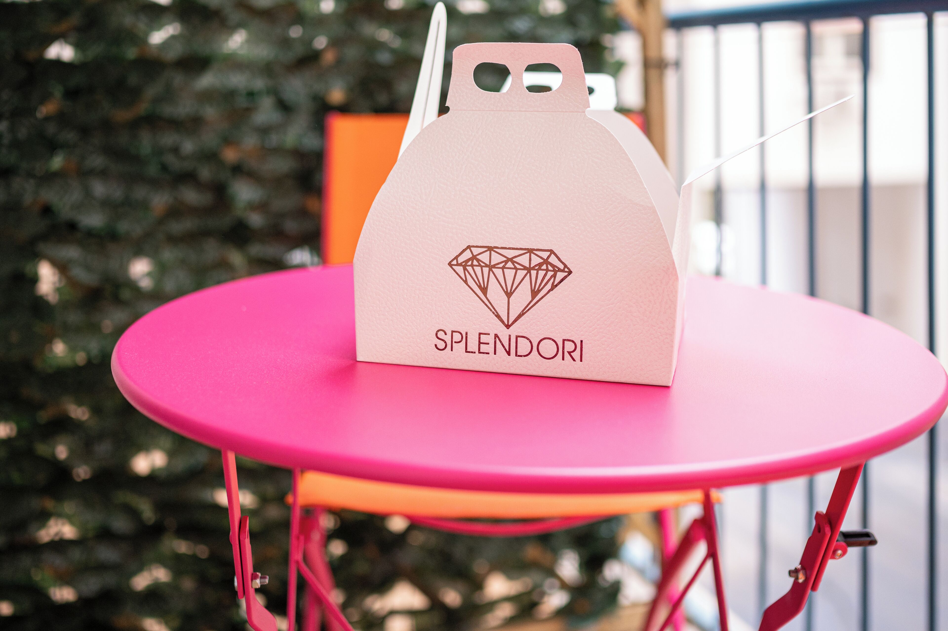 Uma mesa rosa com uma sacola de papel da marca Splendorii em cima.