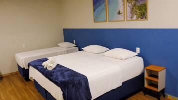 Quarto de hotel com duas camas de solteiro, cabeceira azul, roupa de cama branca e uma pequena mesa de cabeceira de madeira.