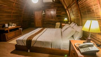 Um quarto aconchegante com piso de madeira, uma cama grande, um abajur e um telefone sobre uma mesinha de cabeceira de madeira.