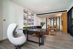 Uma sala de estar moderna com uma poltrona branca curva, um sofá preto e uma área de jantar com mesa e cadeiras de madeira.