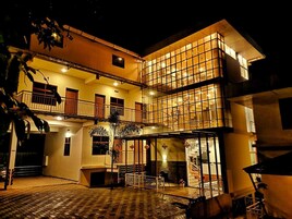 Um edifício de vários andares com uma varanda no andar superior, uma escadaria que leva ao nível superior e uma área externa coberta com piso estampado.