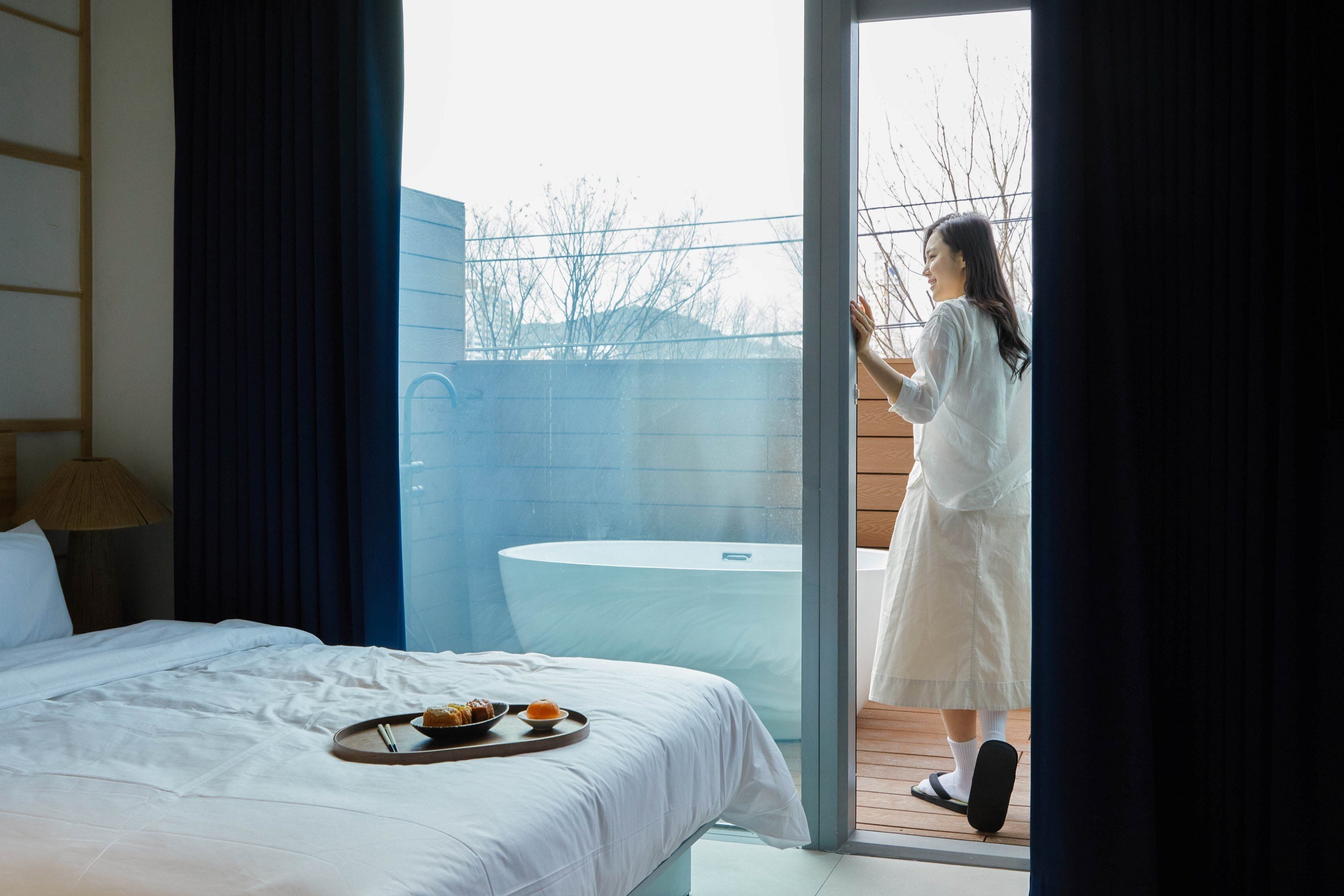 Quarto de hotel com cama, bandeja de comida, banheira e vista para o exterior.