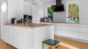 Uma cozinha moderna com armários brancos, bancada de madeira, pia embutida e janela com vista para árvores.
