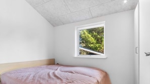 Quarto com cama, janela com vista para árvores, cabeceira de madeira e teto branco.