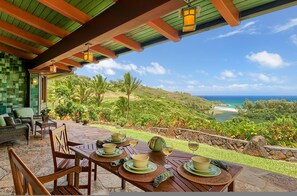 Espaço de refeições com mesa posta para quatro pessoas, com vista para uma praia e oceano.