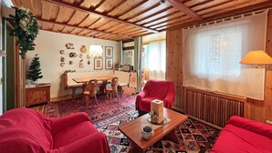 Um quarto aconchegante com teto de madeira, uma sala de jantar com mesa e cadeiras, um sofá vermelho e um tapete estampado.