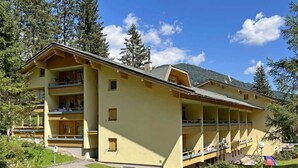 Um hotel com vários andares, varandas, área de estar coberta ao ar livre e montanhas ao fundo.
