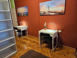 Um quarto com duas escrivaninhas, uma cadeira, uma estante e duas pinturas na parede.