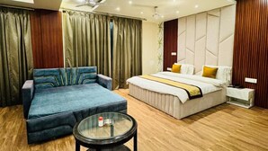 Quarto de hotel moderno com sofá, cama, mesa de centro de vidro e ventilador de teto.